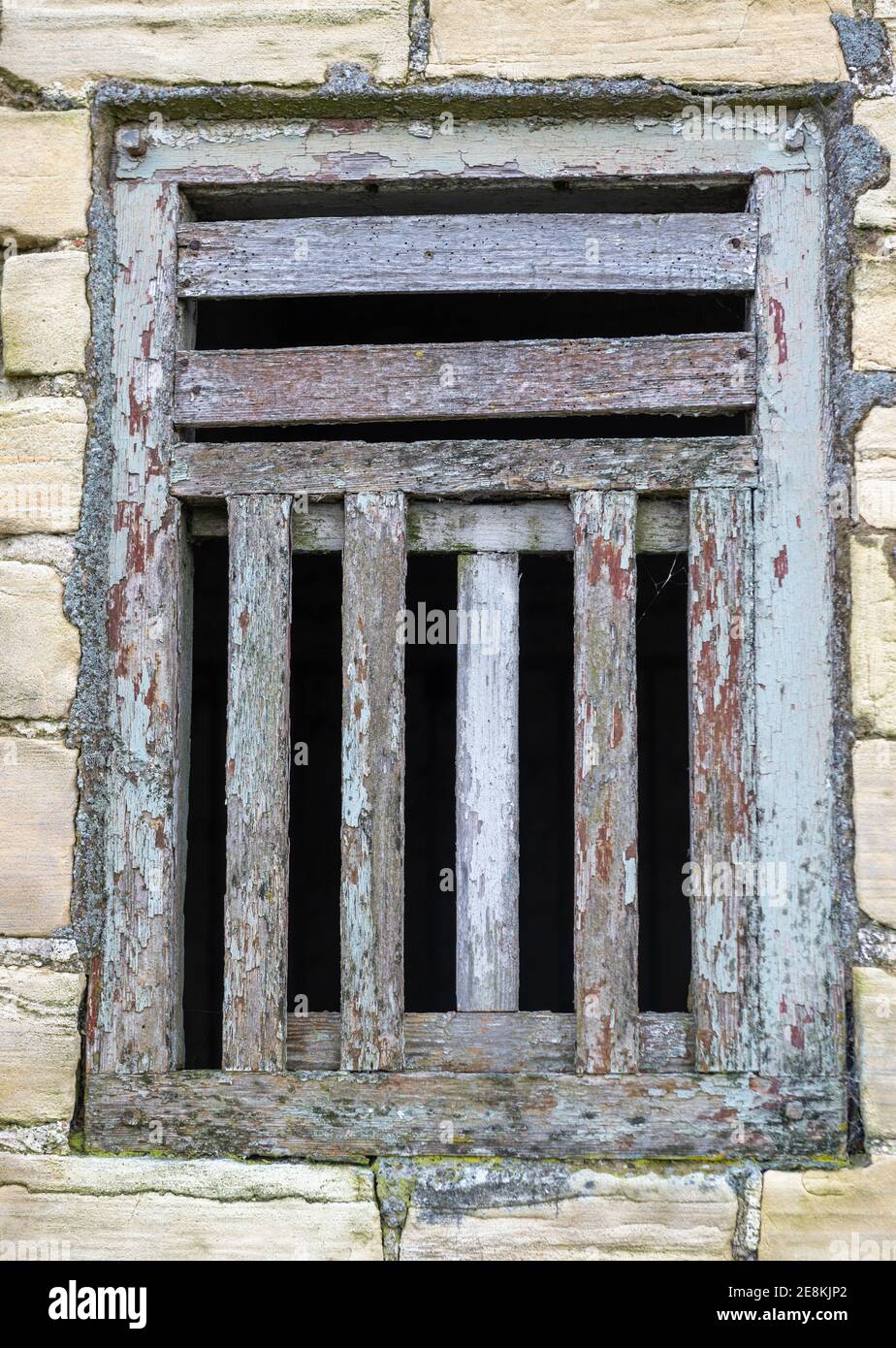 Old wood framed and barred window with peeling paint in a stone barn ...