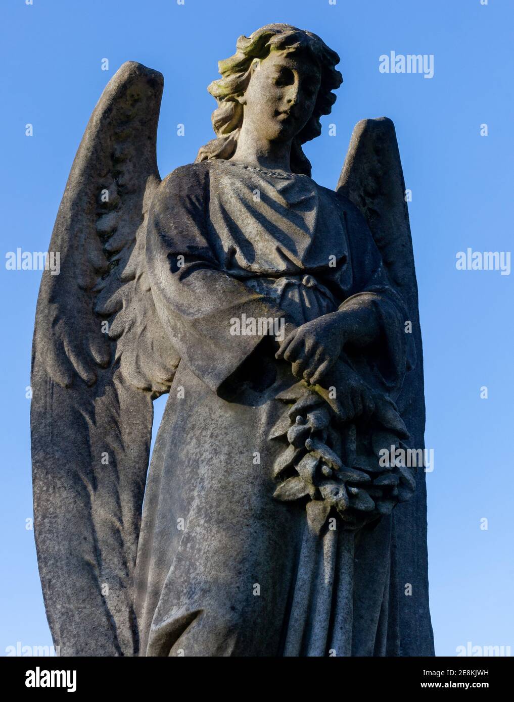sunlit carved stone angel grave marker in a cemetery set against a blue ...