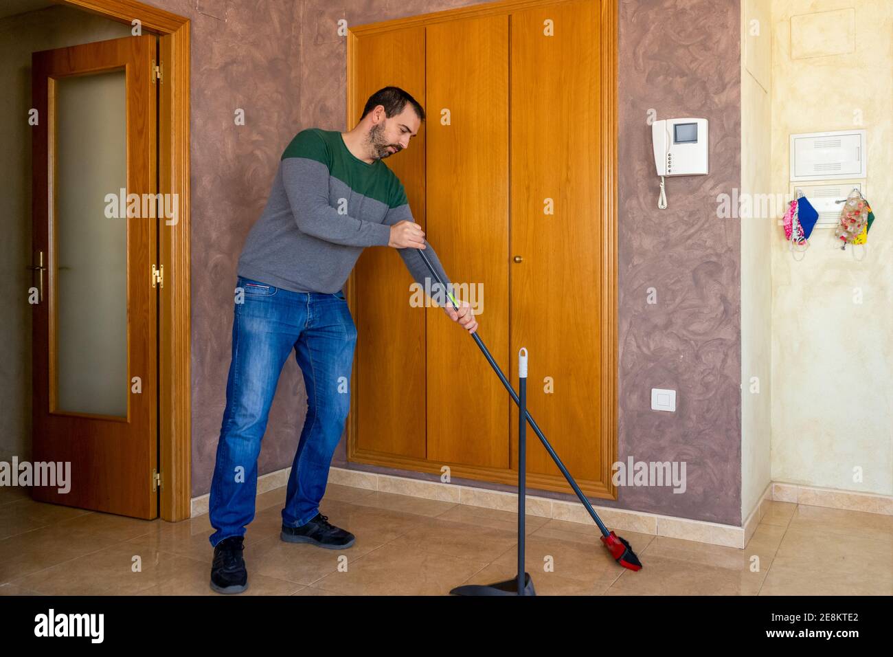 Bearded man sweeping the ceramic floor of his house. Selective focus ...