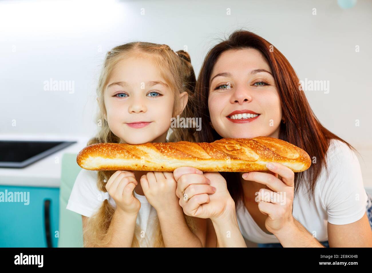 Happy family, mom and daughter eat one bread biting from different ...