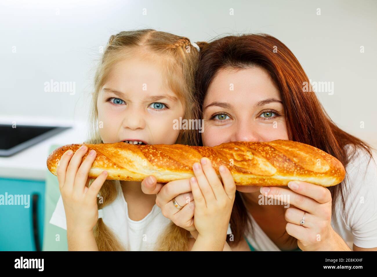 Happy family, mom and daughter eat one bread biting from different ...
