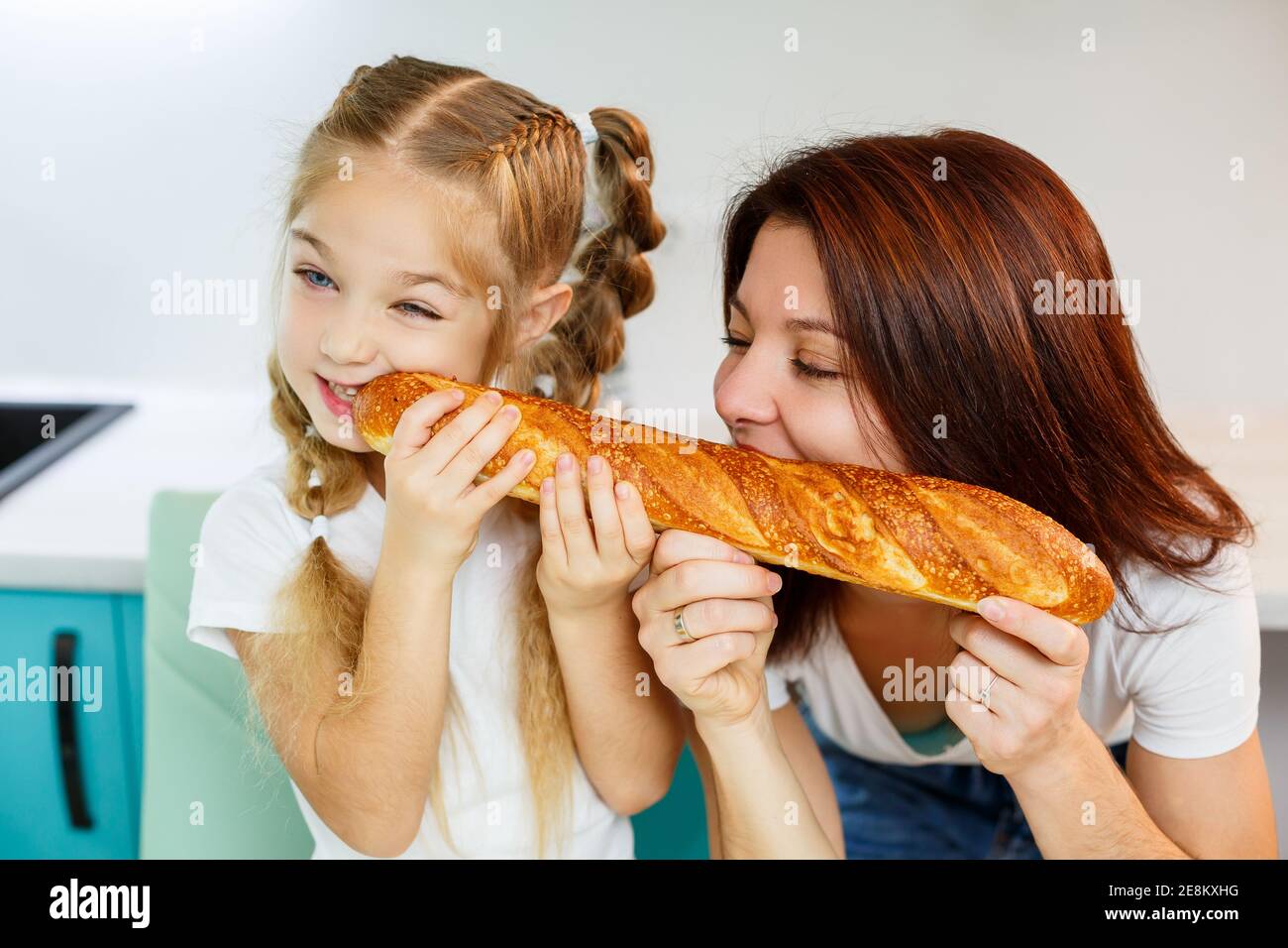 Happy family, mom and daughter eat one bread biting from different ...