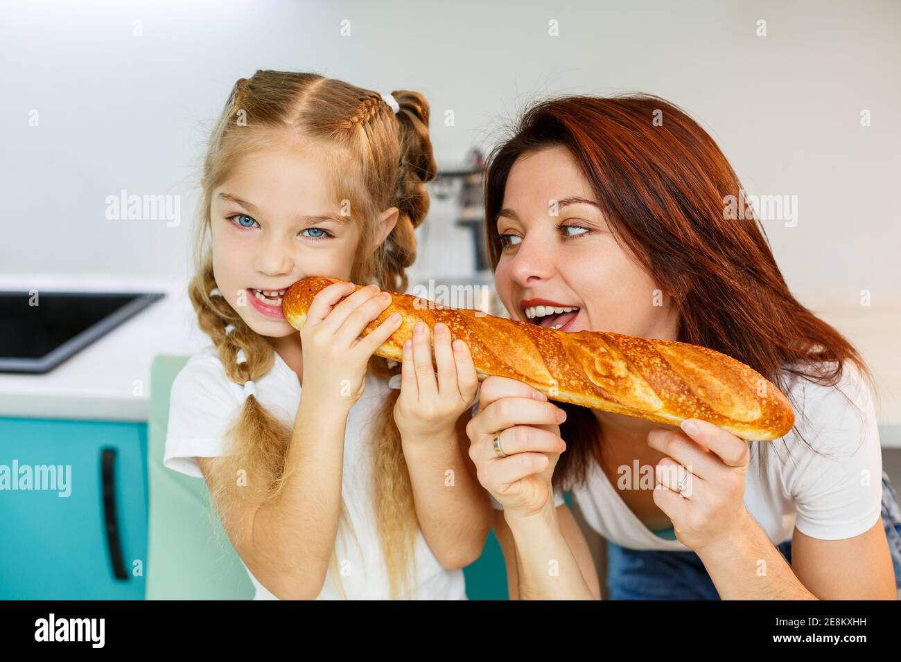 Happy family, mom and daughter eat one bread biting from different ...