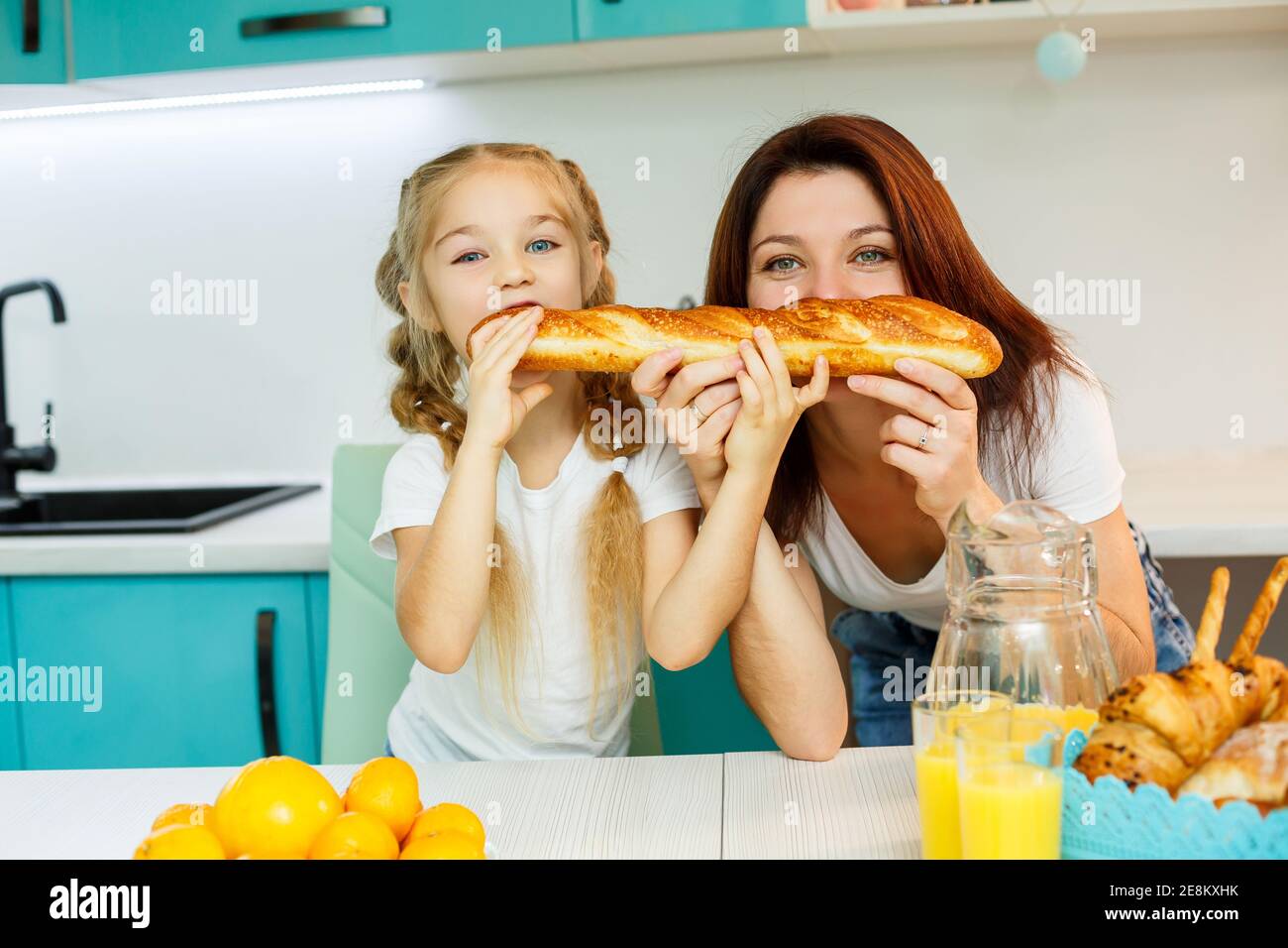 Happy family, mom and daughter eat one bread biting from different ...