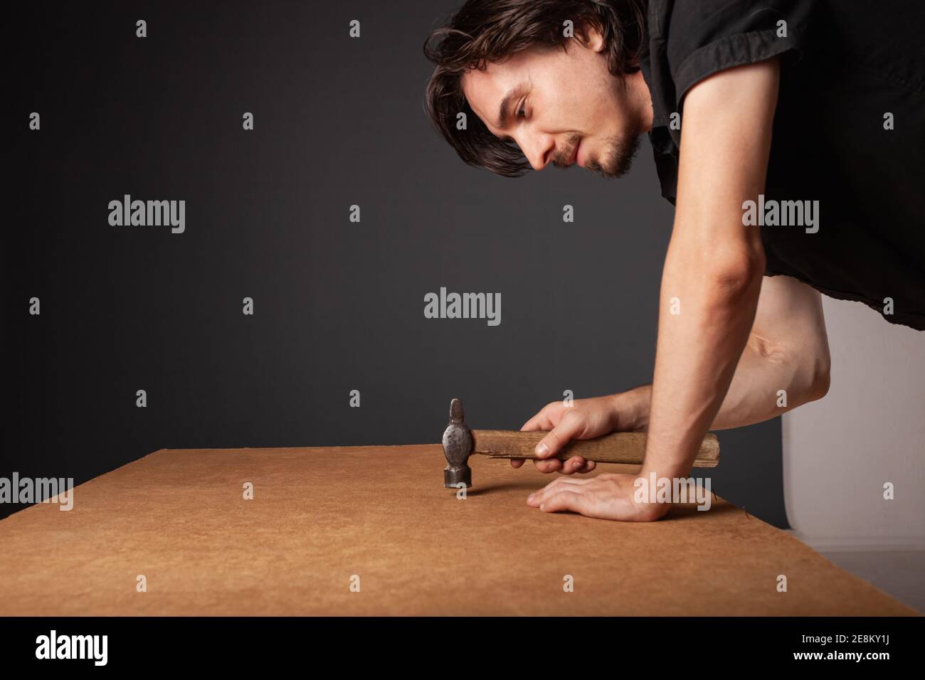 A man hammers nails into a cupboard. The back wall of the cupboard is ...