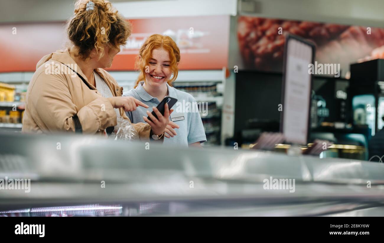 Happy grocery store employee helping female customer. Young employee ...
