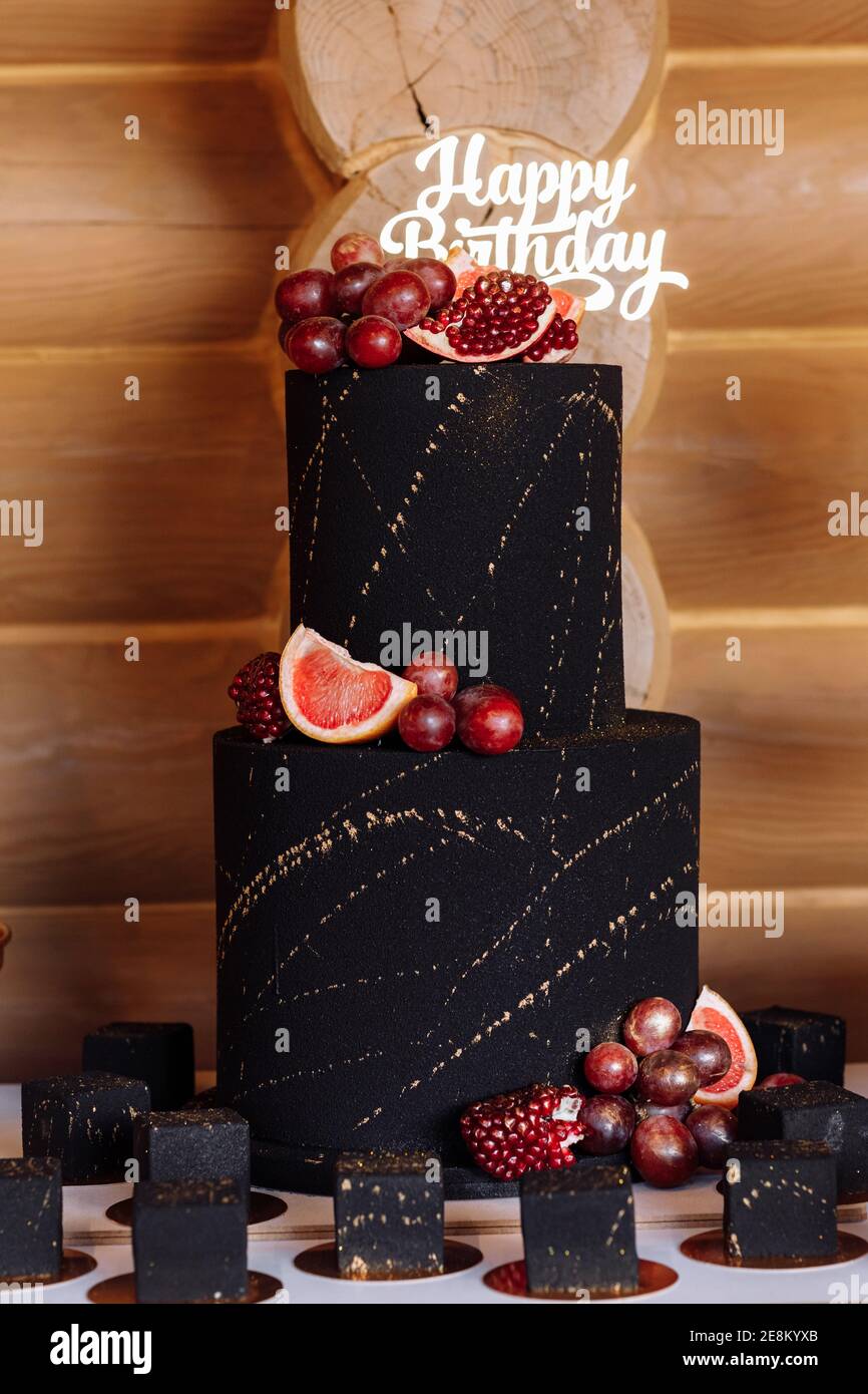 big black birthday cake with fresh fruits and sweets on a festive table ...