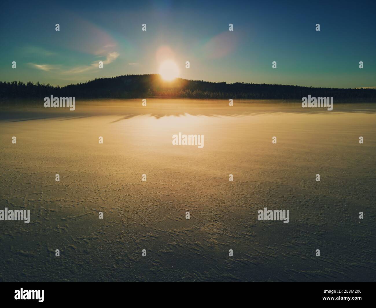 Sunset over the snowy ice of a frozen lake in the wild. Frozen cold fog ...