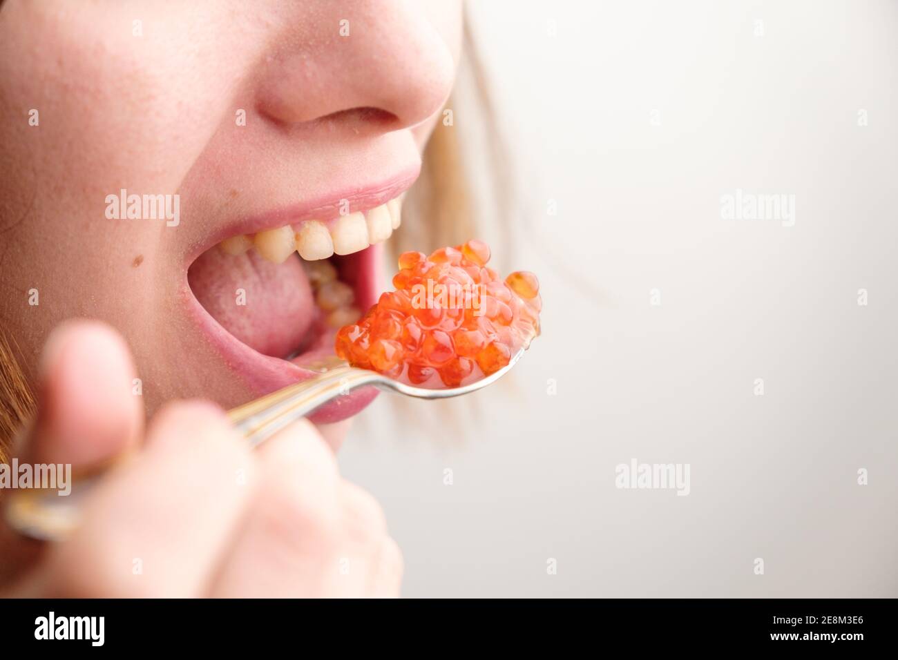 Young beauty woman eating a red caviar by spoon on the white background ...