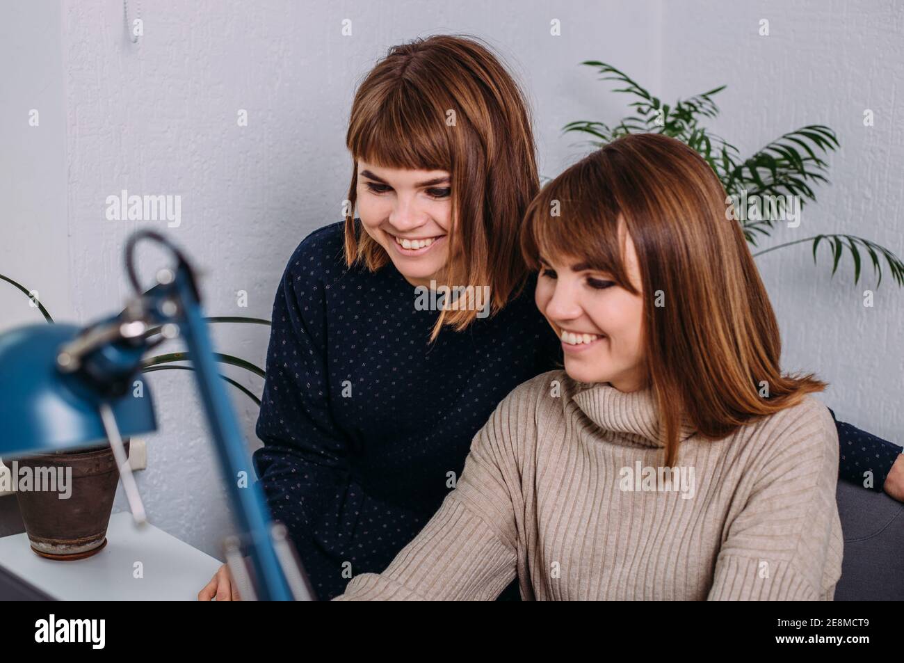 Two girls twins work side by side in the office on a laptop ...