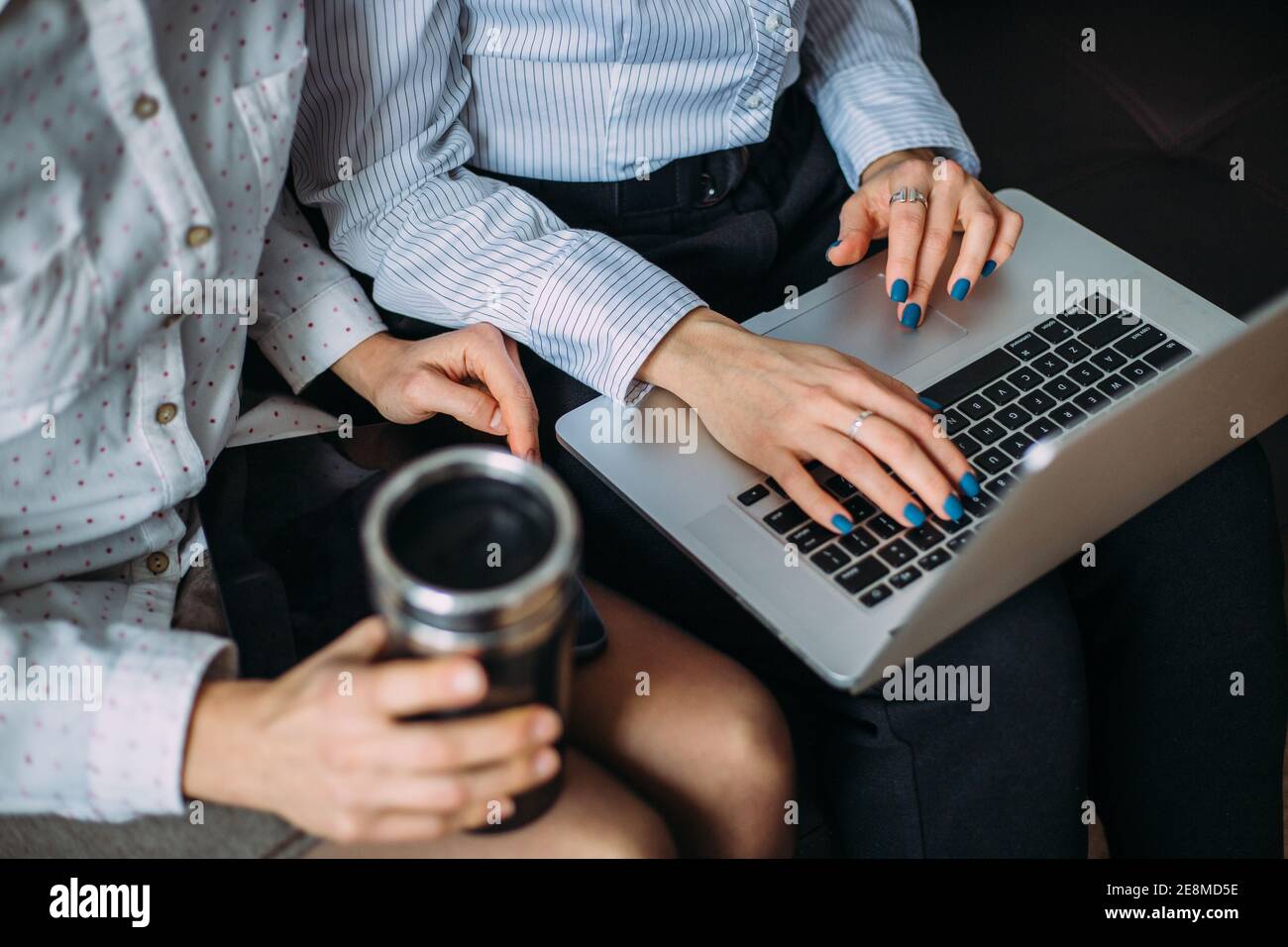 Two girls work side by side in the office on a laptop. Interaction of ...