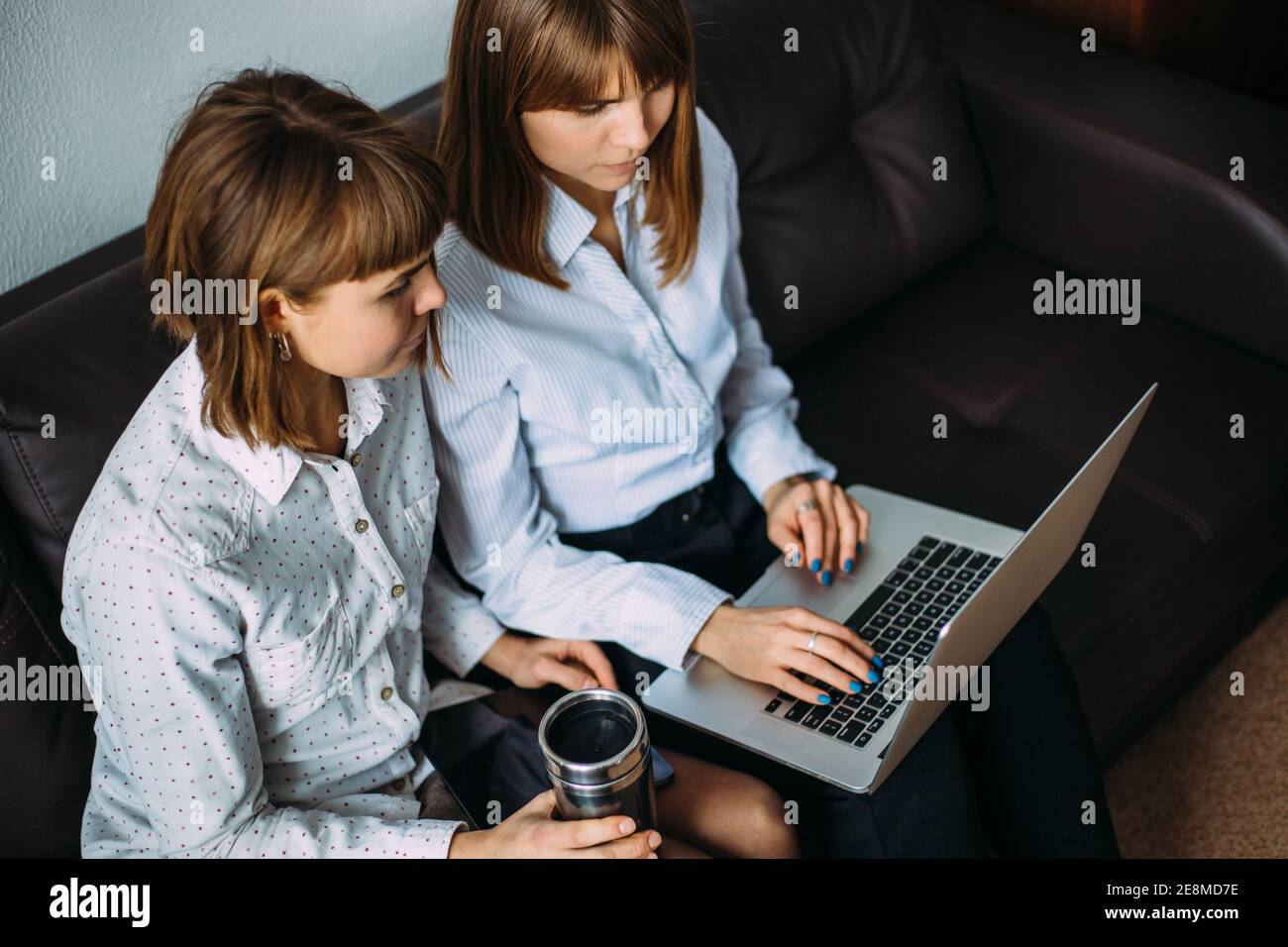 Two girls twins work side by side in the office on a laptop ...