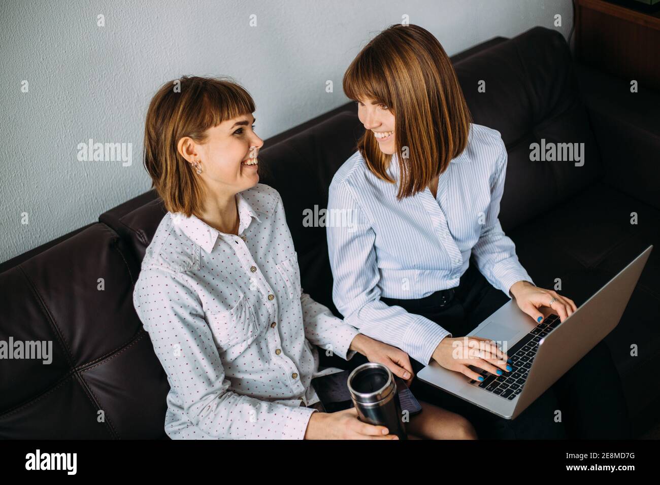 Two girls twins work side by side in the office on a laptop ...
