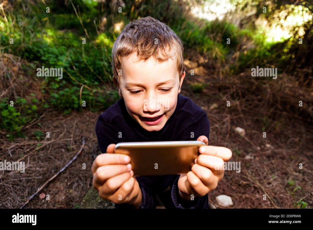 Happy child plays with his mobile phone during an excursion to nature ...
