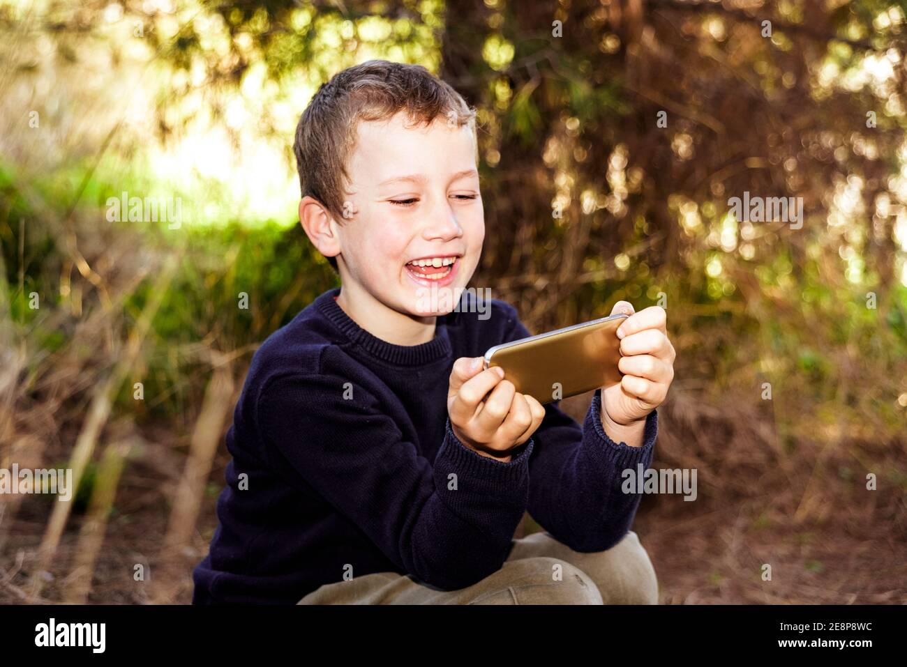 Happy child plays with his mobile phone during an excursion to nature ...