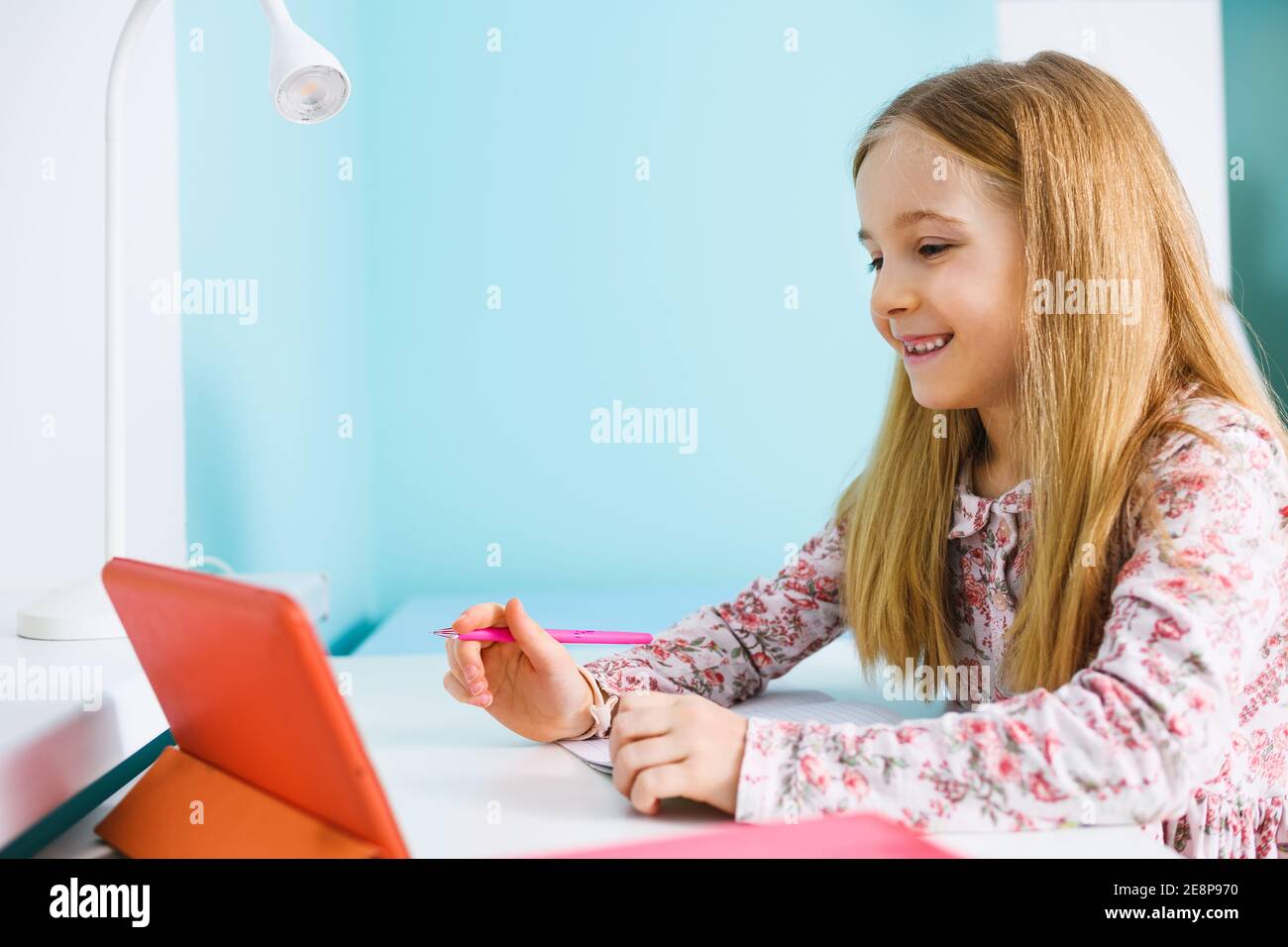 Elementary school age girl sit at desk and smiling for tablet screen ...