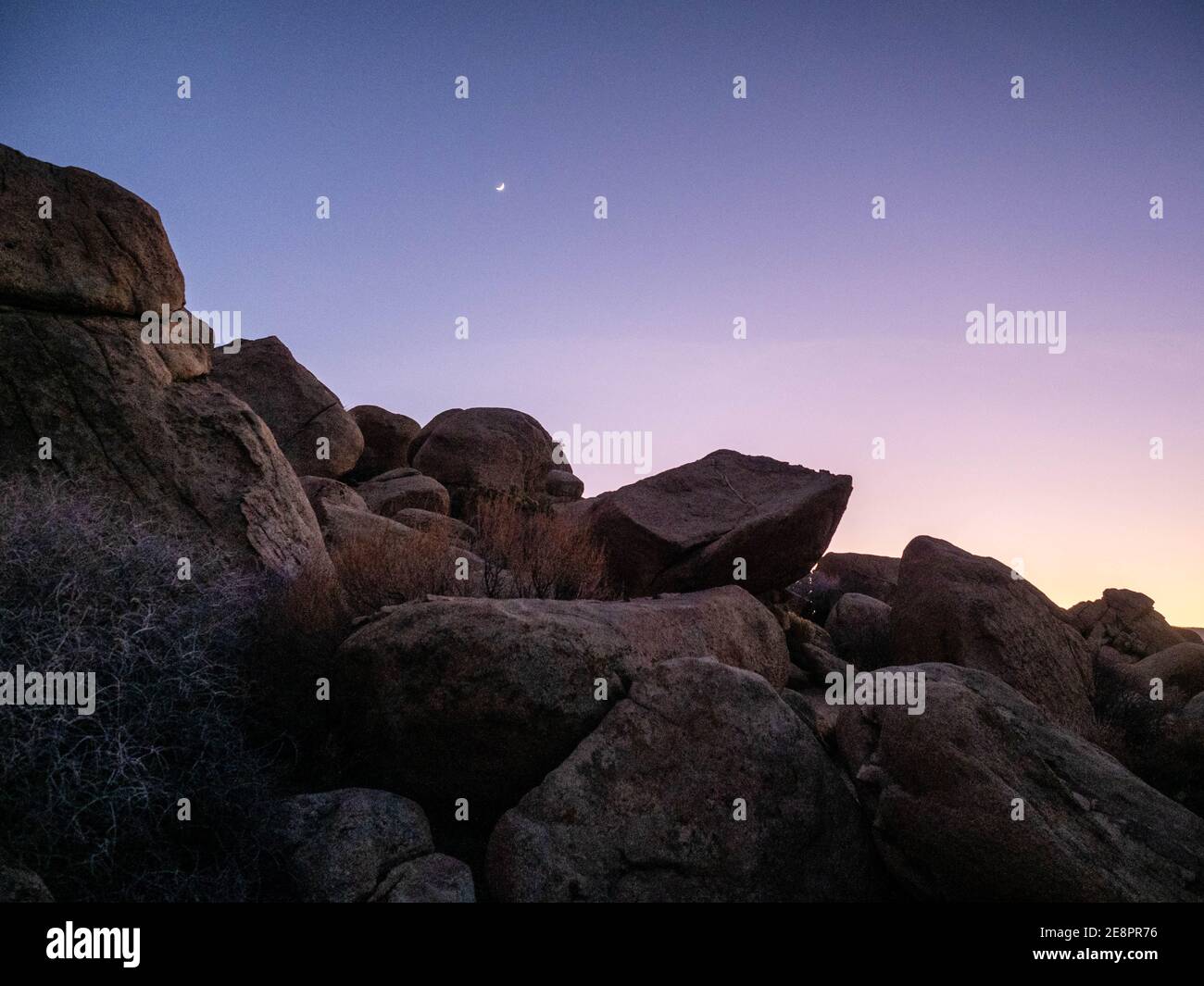Field of boulders at dusk with sunset sky and crescent moon in Yucca ...