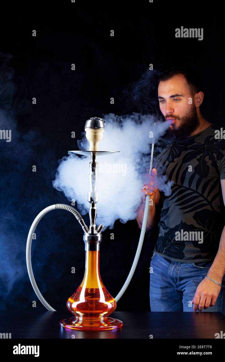 Bearded young man smoking shisha in a dark night club Stock Photo - Alamy