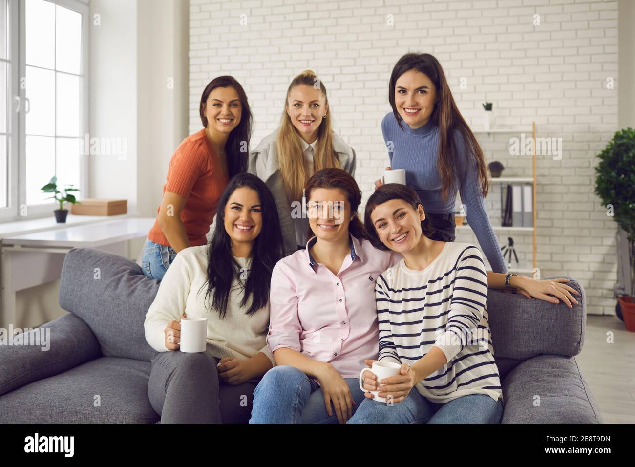 Group of happy young women sitting on couch, enjoying tea, smiling and ...