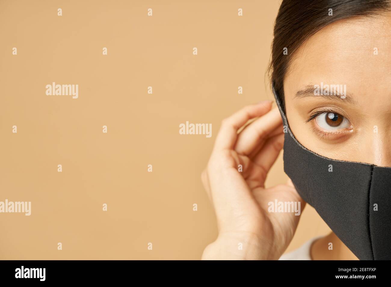 Half face shot of young woman putting on black facial mask, staying ...