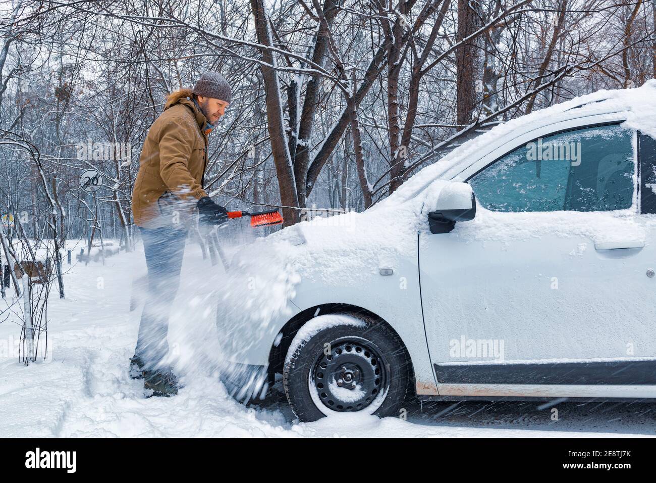 The driver brushes snow off the hood of the car after heavy snowfall ...