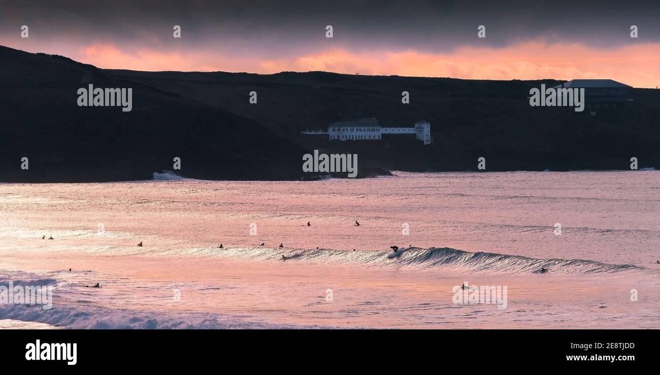 A panoramic view of the sun setting over surfers in Fistral Bay in ...