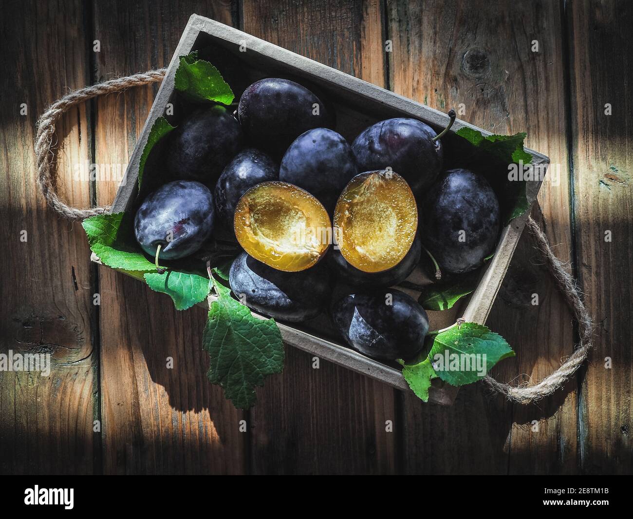 Fresh harvested plums with sliced one in wooden box on wooden table ...