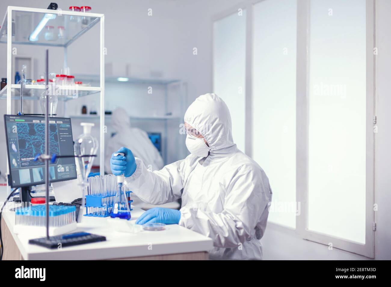 Microbiologist dressed in coverall using automatic pipette in ...
