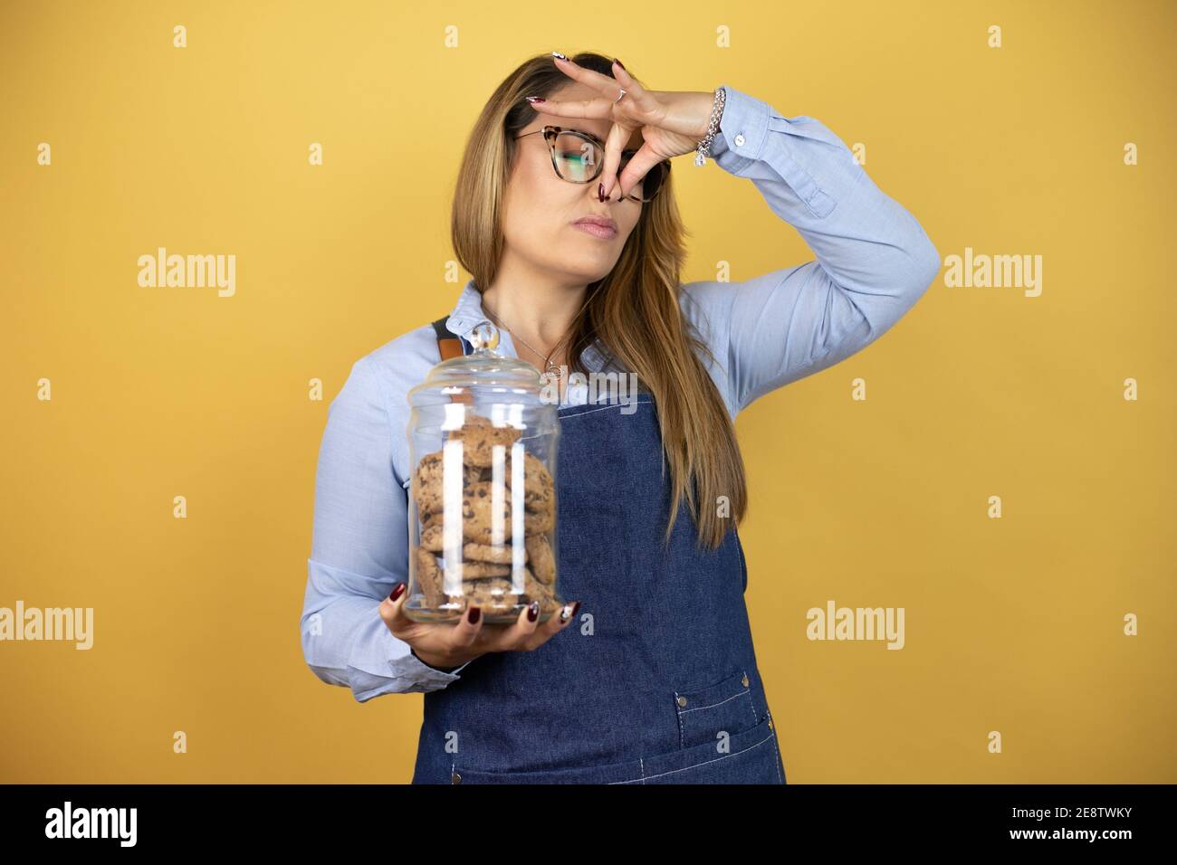 Young hispanic woman wearing baker uniform holding a cookies jar ...