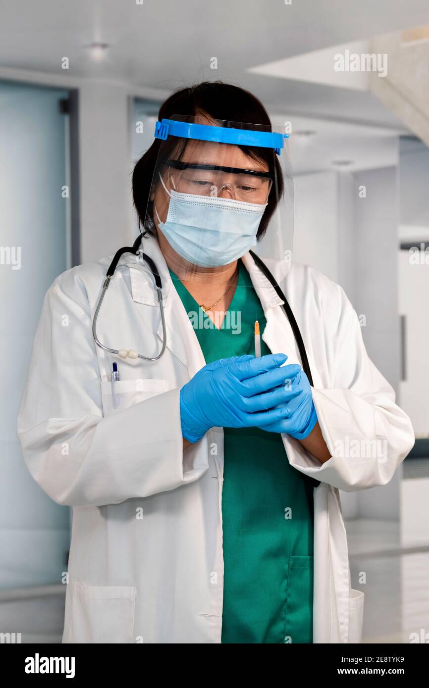 Asian female doctor with face shield and gloves holding a syringe with ...