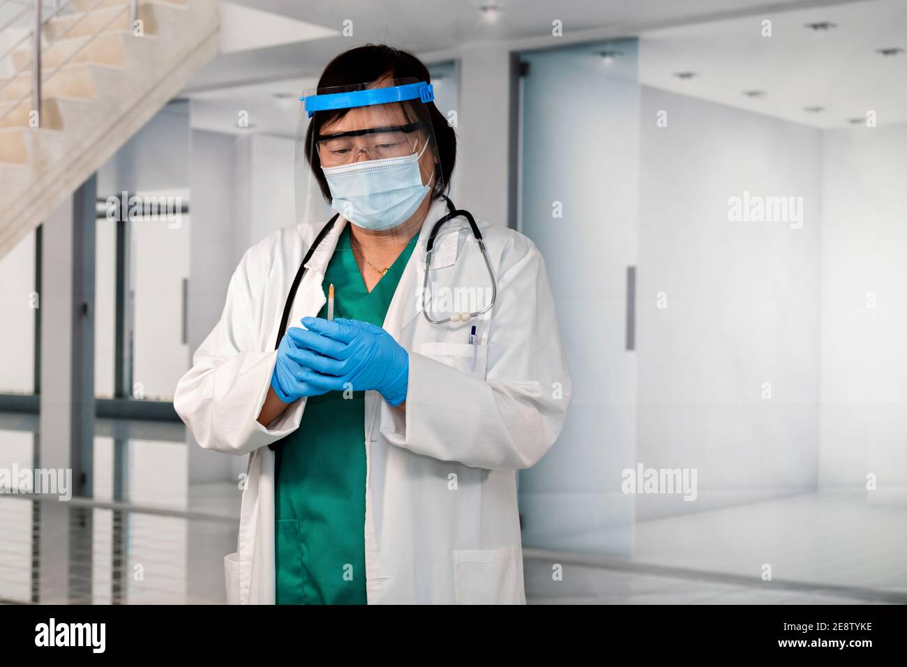 Asian female doctor with face shield and gloves holding a syringe with ...