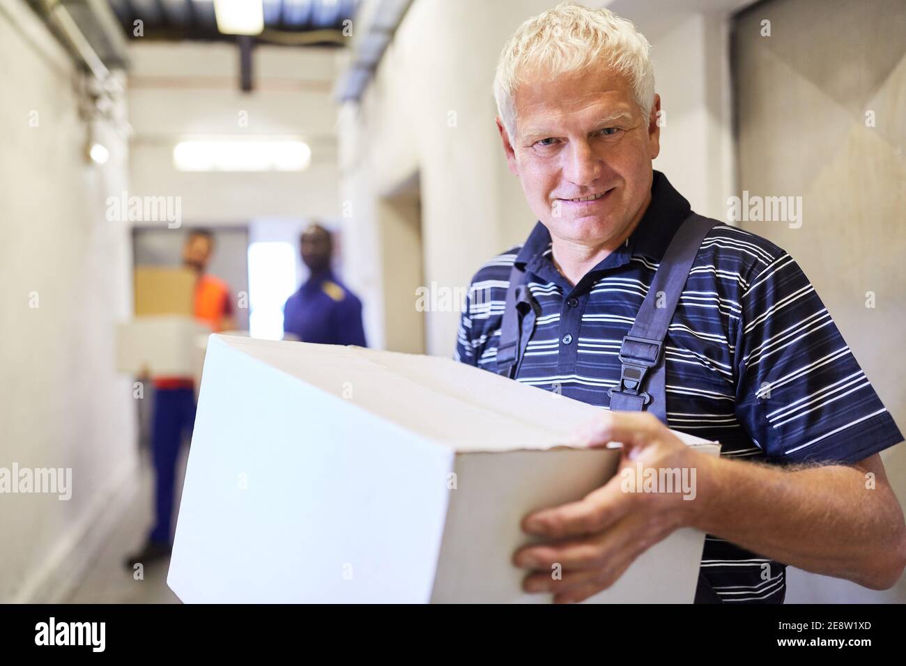 Older worker as mini jobber carries cardboard box through aisle to the ...