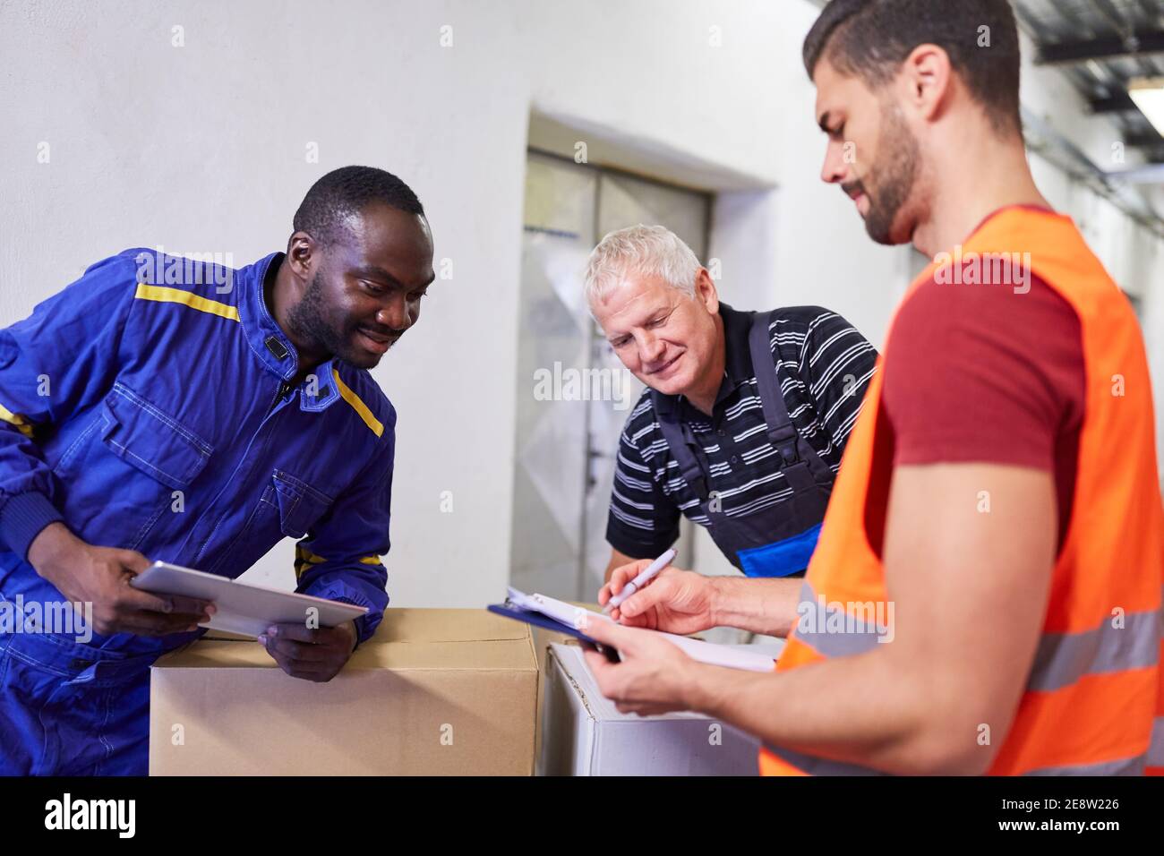 Three workers checking a delivery of goods with checklist on clipboard ...