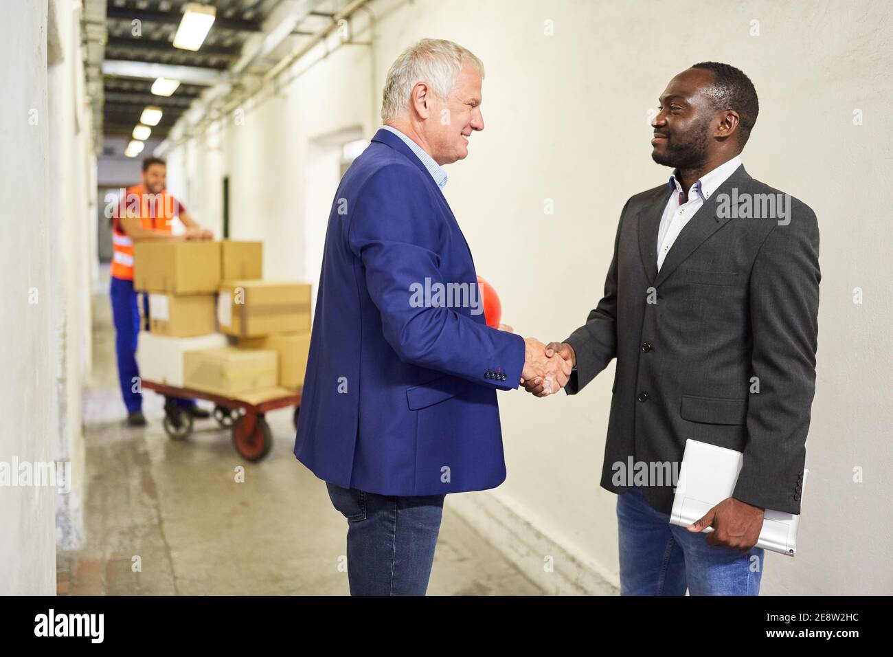 Two businessmen shaking hands in front of workers in the factory with ...