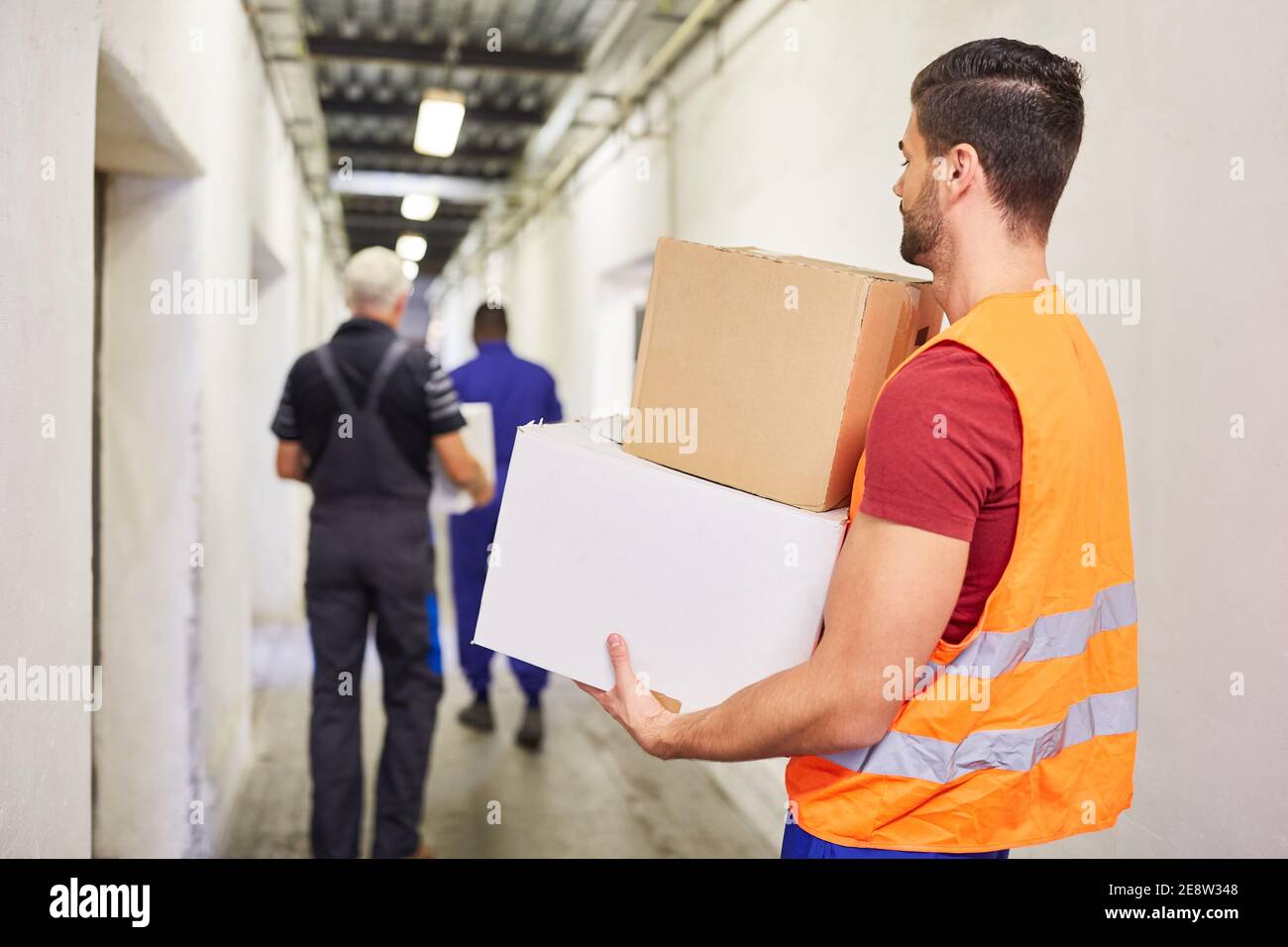 Worker with safety vest carries cardboard boxes through aisle to the ...