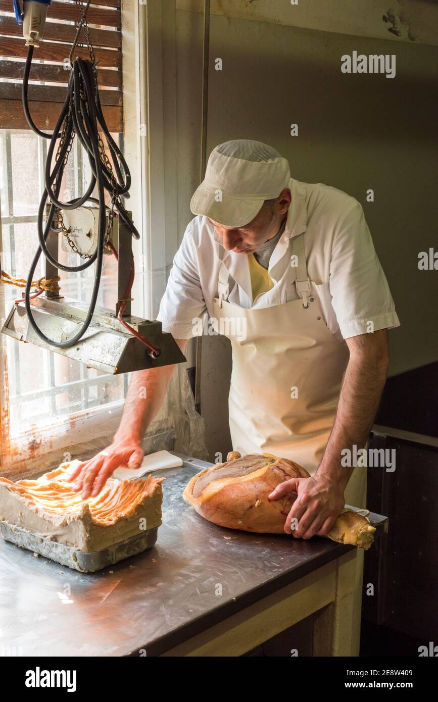 A man worker in a parma ham factory adding fat by hand to seal the meat ...