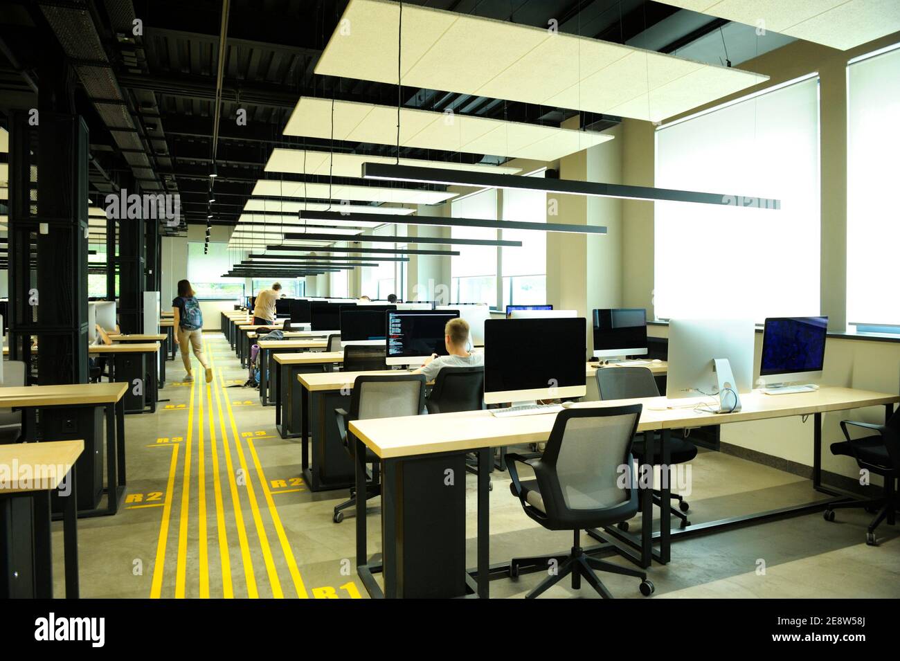 Large computer room with laptops on tables, blurred people working at ...