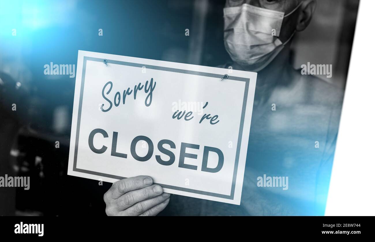 Store owner holding sorry we're closed sign behind the window; light ...