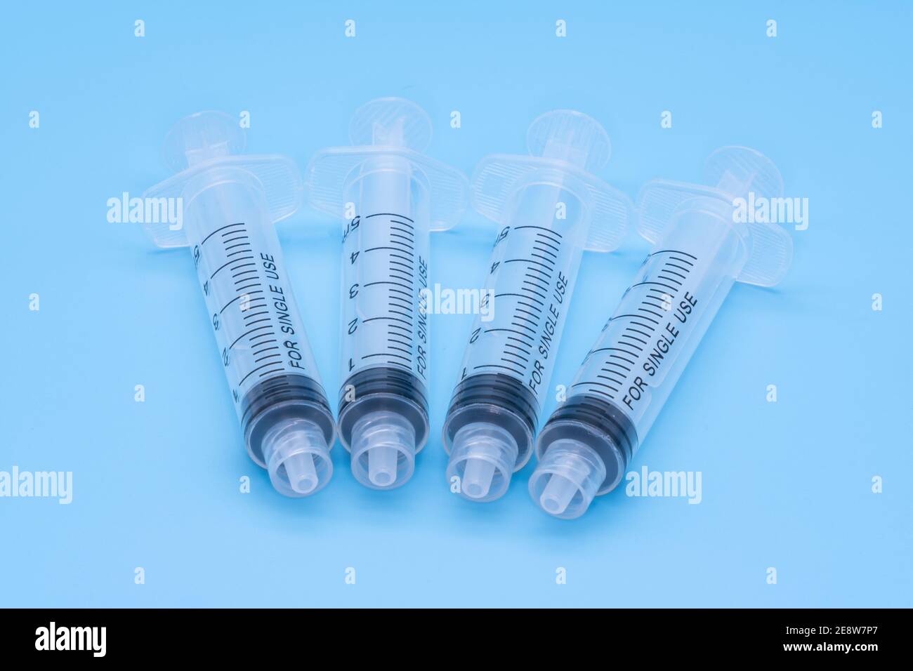Four clear plastic 5ml syringes isolated against a light blue ...