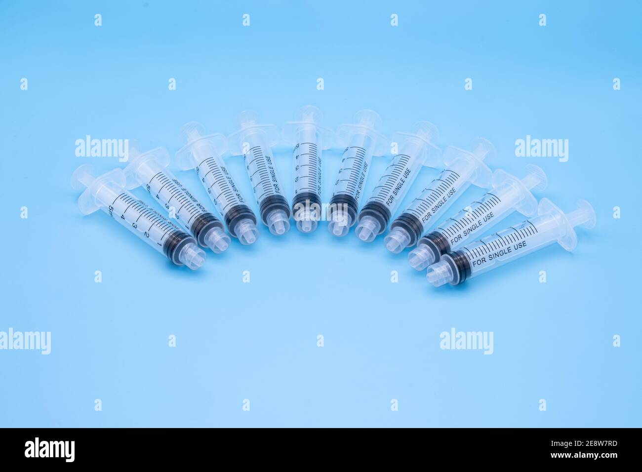 multiple clear plastic 5ml syringes isolated against a light blue ...