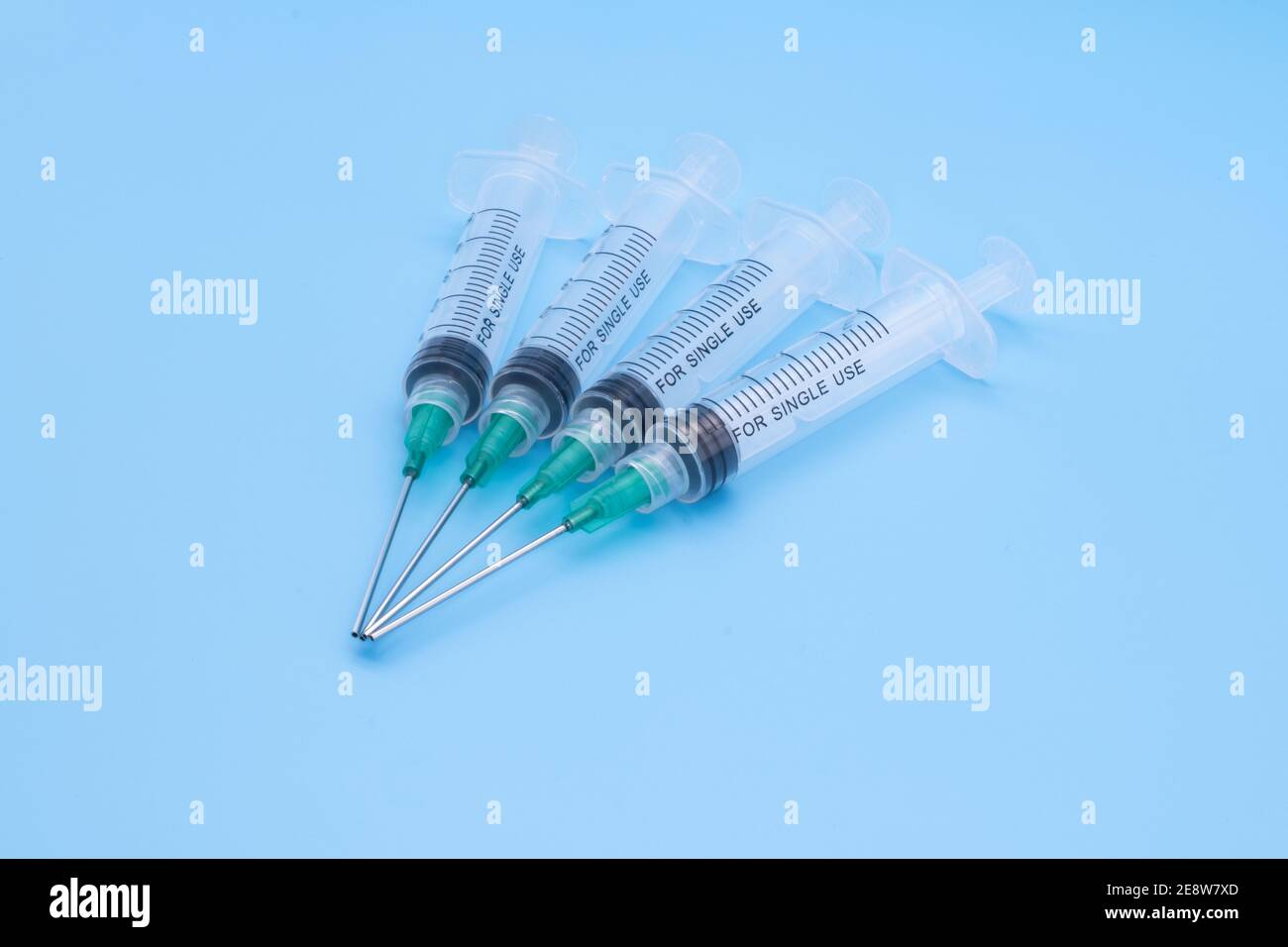 Clear plastic syringes with needles isolated against a light blue ...