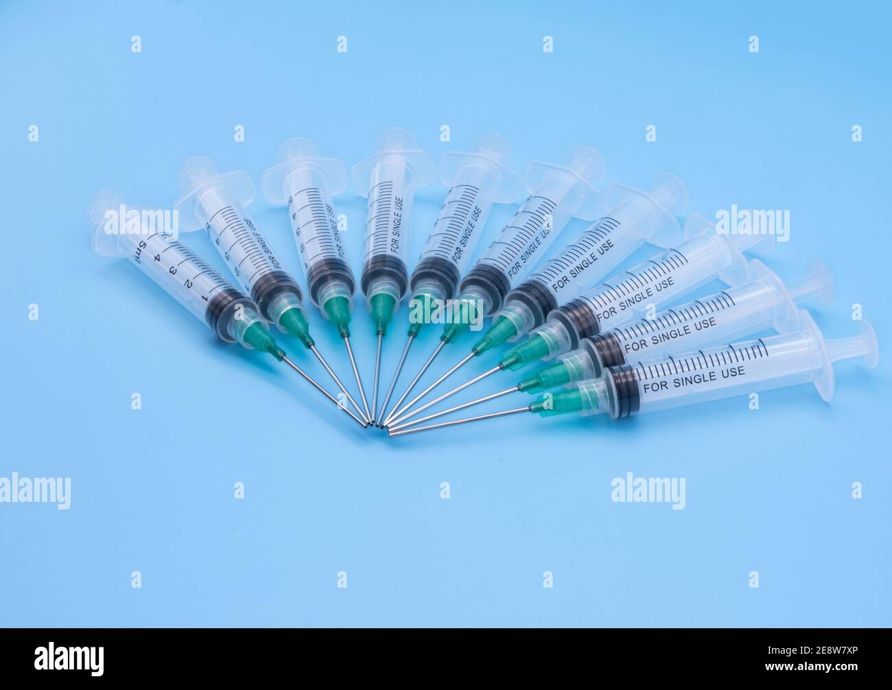 Clear plastic syringes with needles isolated against a light blue ...
