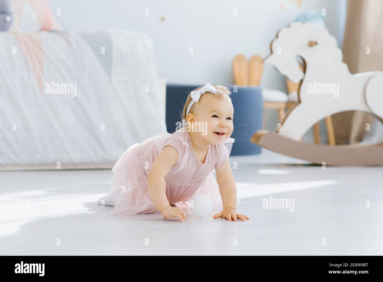 A pretty blue eyed blonde one year old in a pink dress crawls on all ...