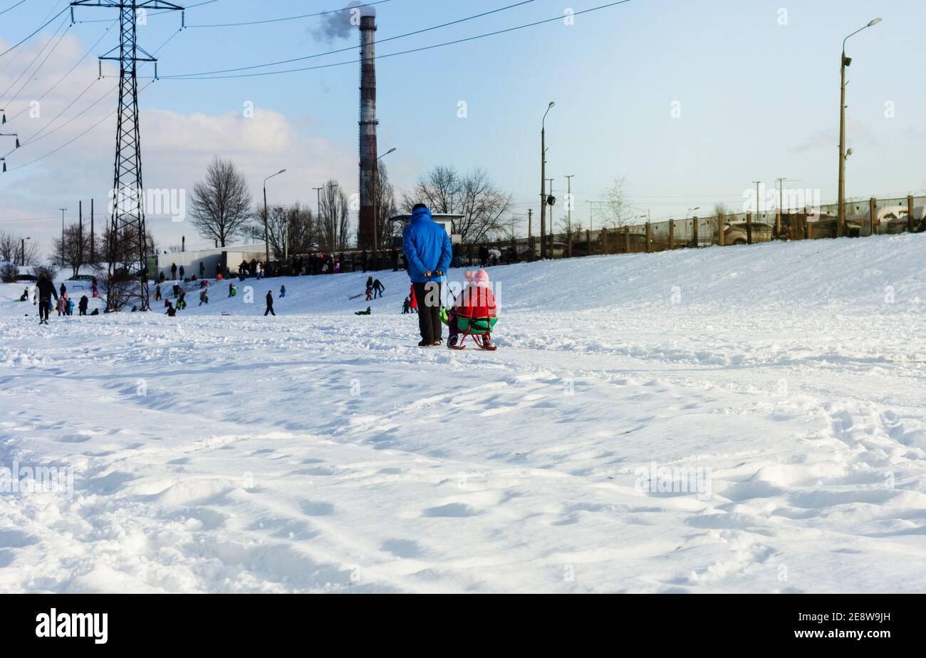 Children and their parents sledding from a snow slide in a city park ...