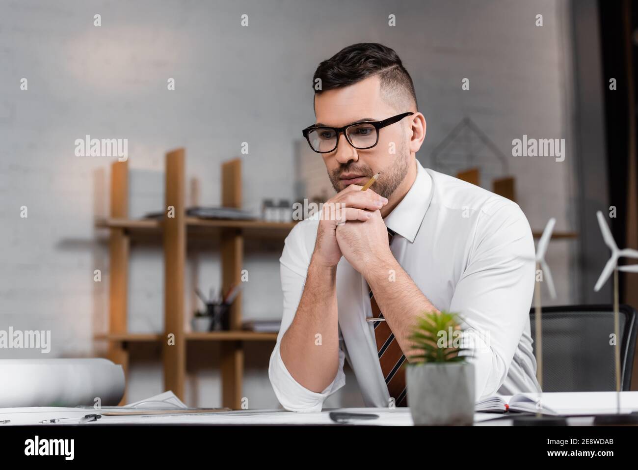 thoughtful architect sitting at workplace near models of wind turbines ...