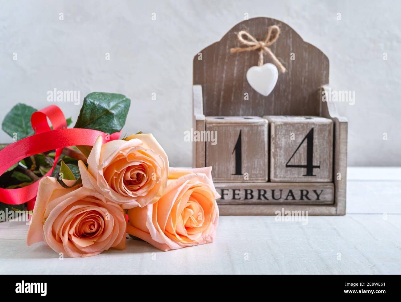 Wooden perpetual calendar on date February 14 and a bouquet of roses ...