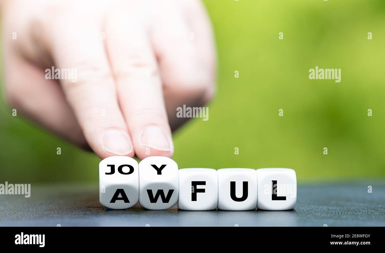 Hand turns dice and changes the word awful to joyful Stock Photo - Alamy