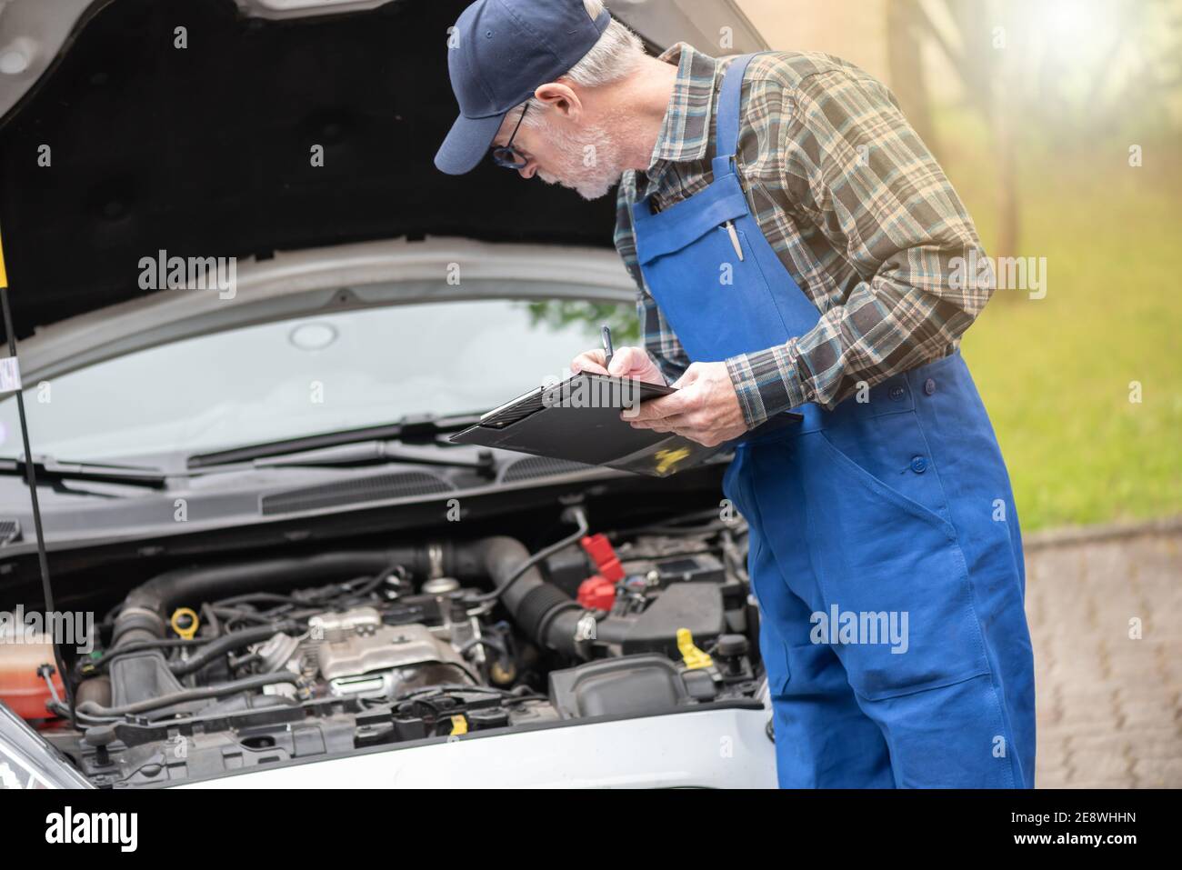 Car mechanic checking a car engine and writing on clipboard Stock Photo ...
