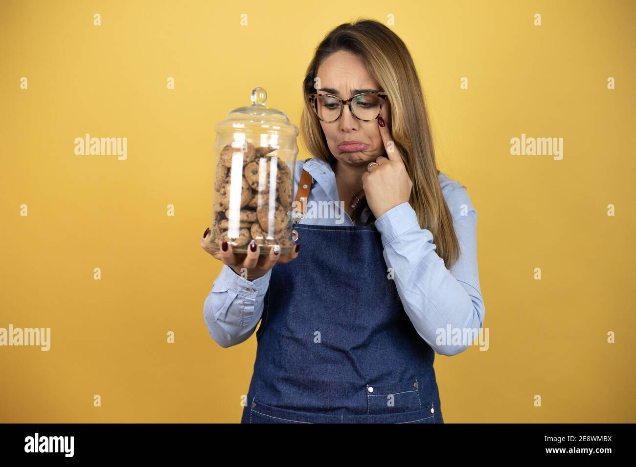 Young hispanic woman wearing baker uniform holding a cookies jar ...
