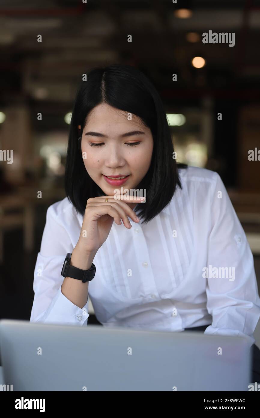 Portrait of young female office worker working on laptop computer in ...
